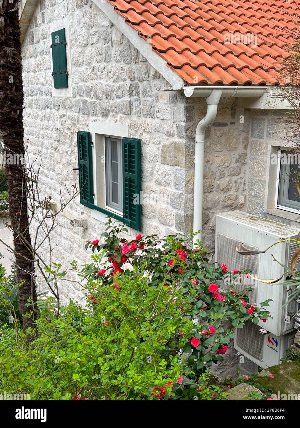 Charming stone house with red tile roof and blooming red flowers ...