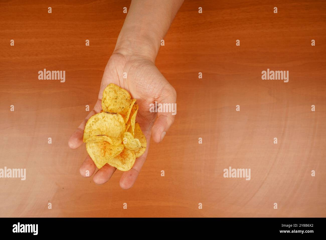 A view of a hand holding a stack of ridged potato chips. Man eating ...