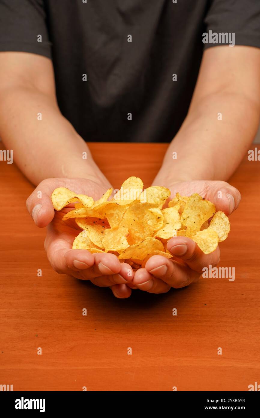 A view of a hand holding a stack of ridged potato chips. Man eating ...