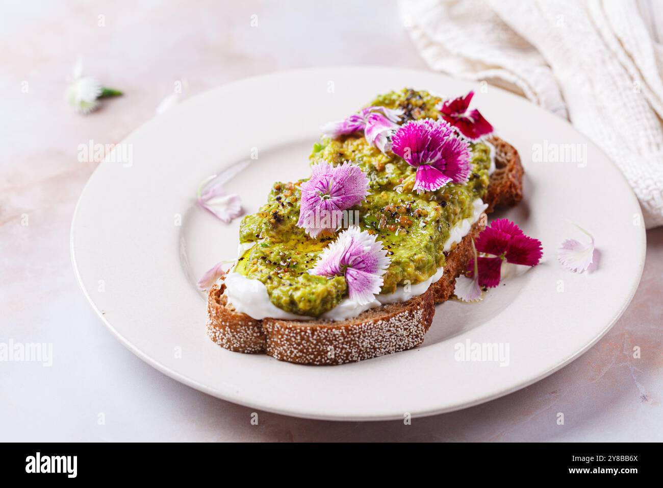 Breakfast avocado toast with pink culinary flowers on plate, on pink ...