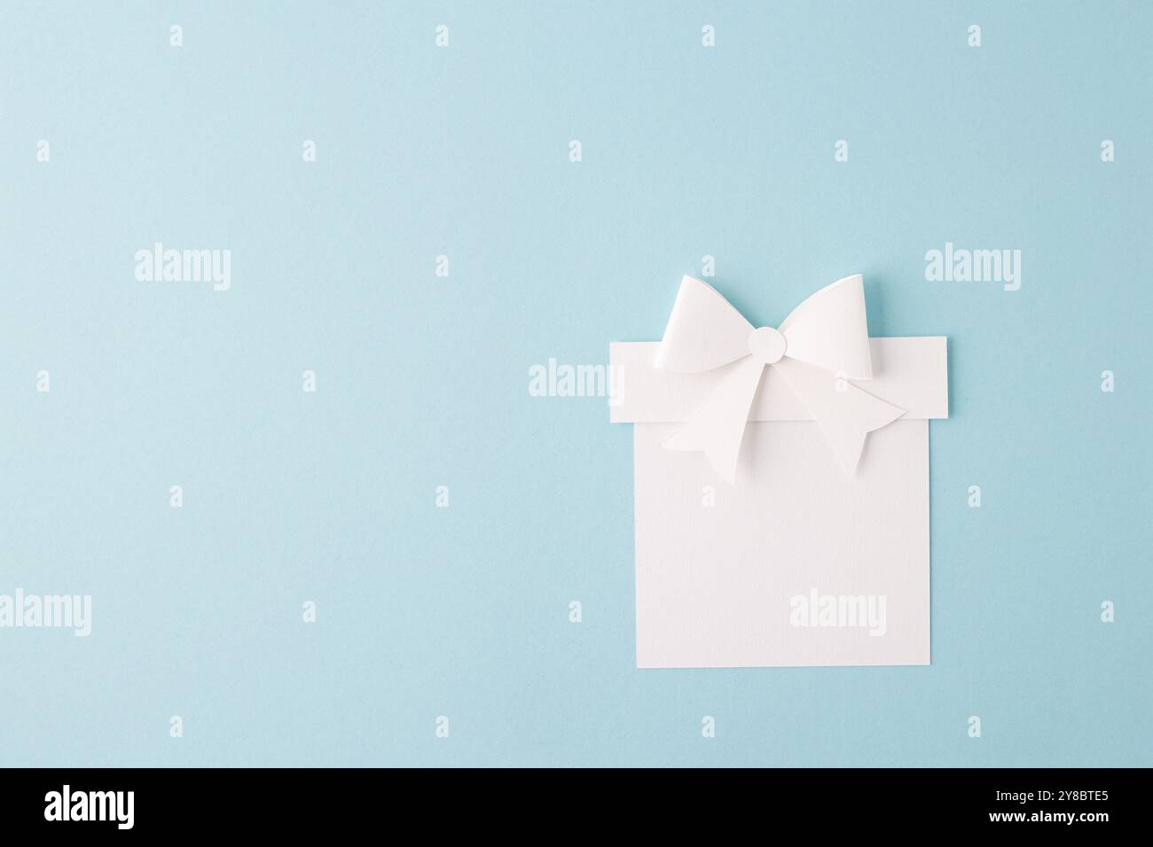 White paper card with bow on light blue background. Elegant ...