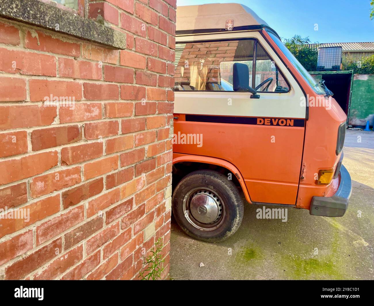an orange devon edition Volkswagen camper van parked next to a red ...