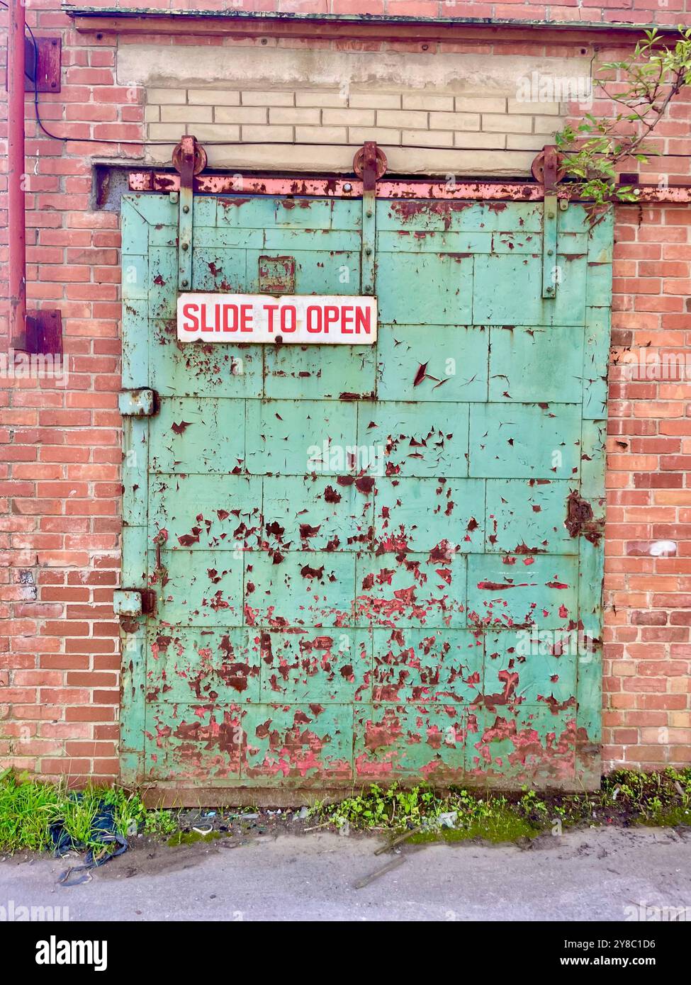 a rusty green metal door with a slide to open instruction sign is the ...