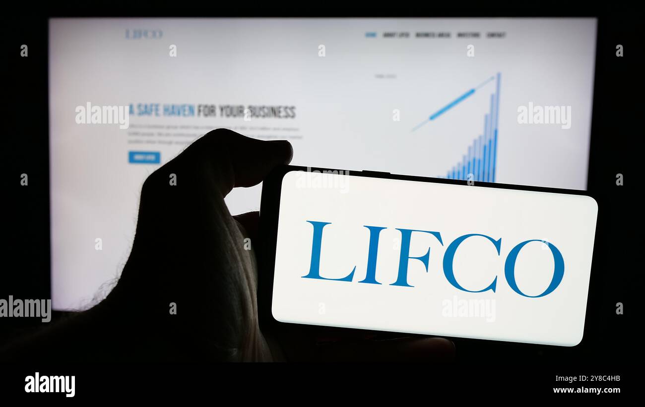Person holding smartphone with logo of Swedish investment company Lifco AB on screen in front of ...
