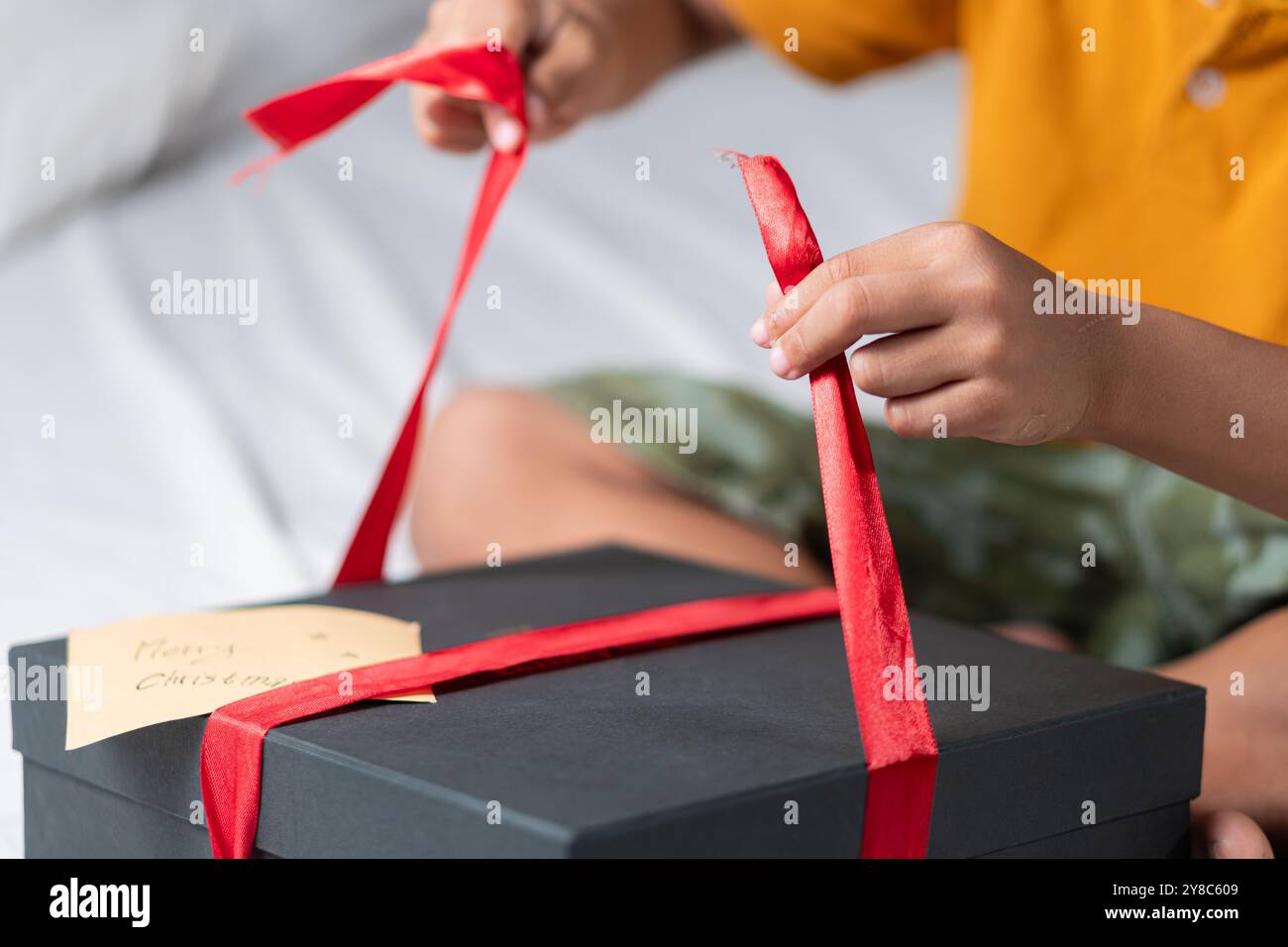A child is unwrapping a Christmas gift, focusing on the red ribbons ...