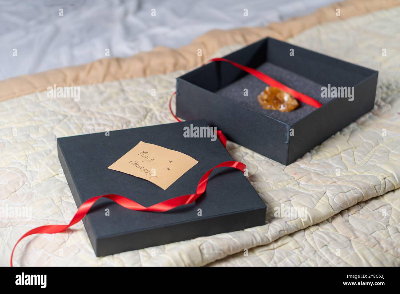 A black gift box with a red ribbon, partially open, revealing a small ...