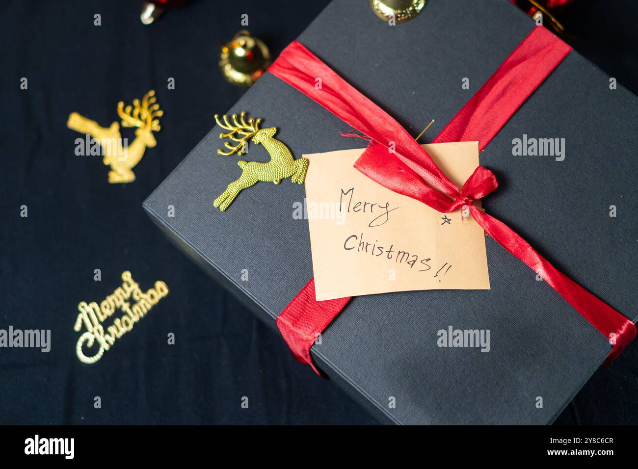 A beautifully wrapped black gift box adorned with a red ribbon and a golden reindeer decoration ...