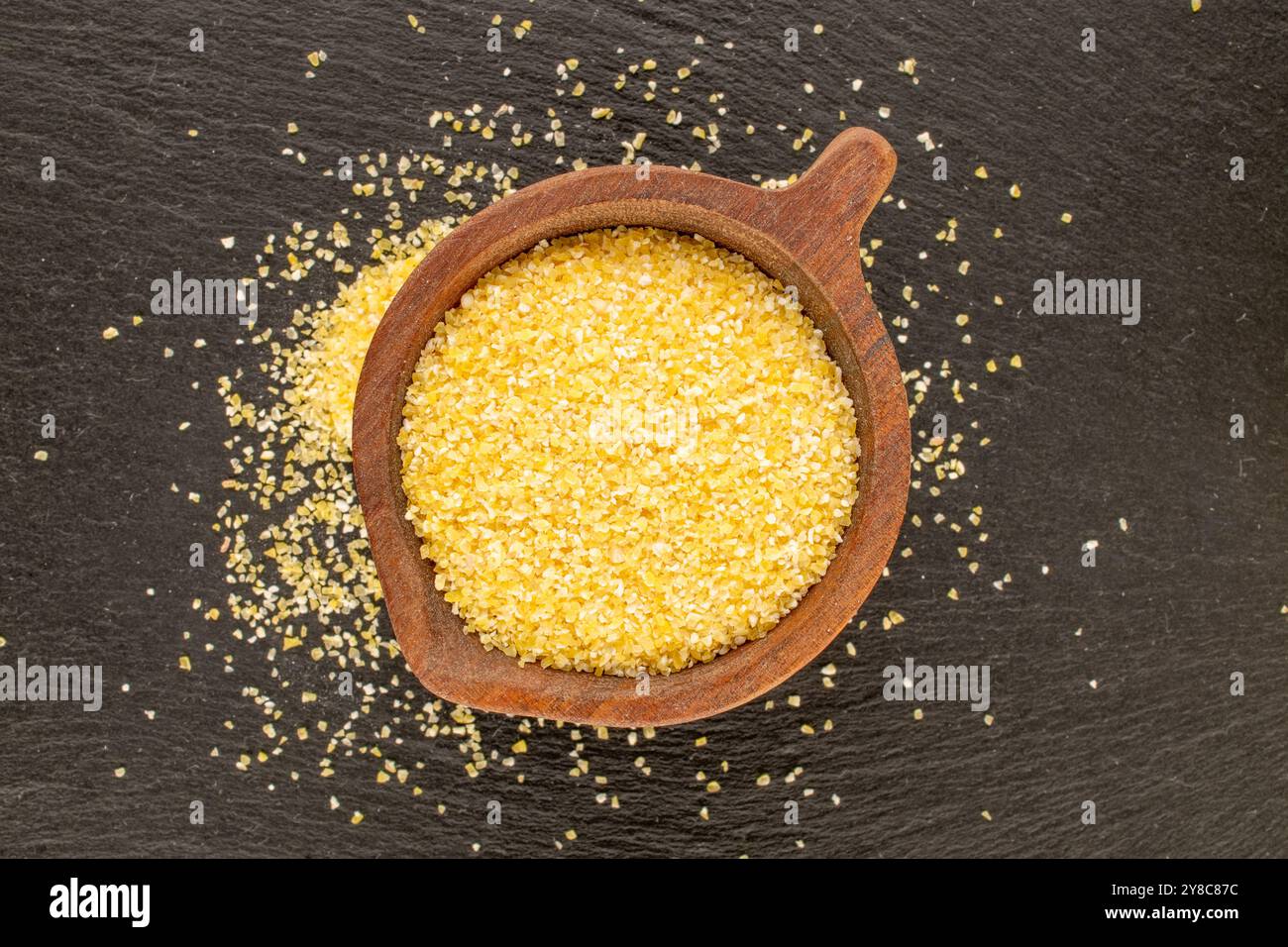 Uncooked corn grits with wooden cup on slate stone, macro, top view ...