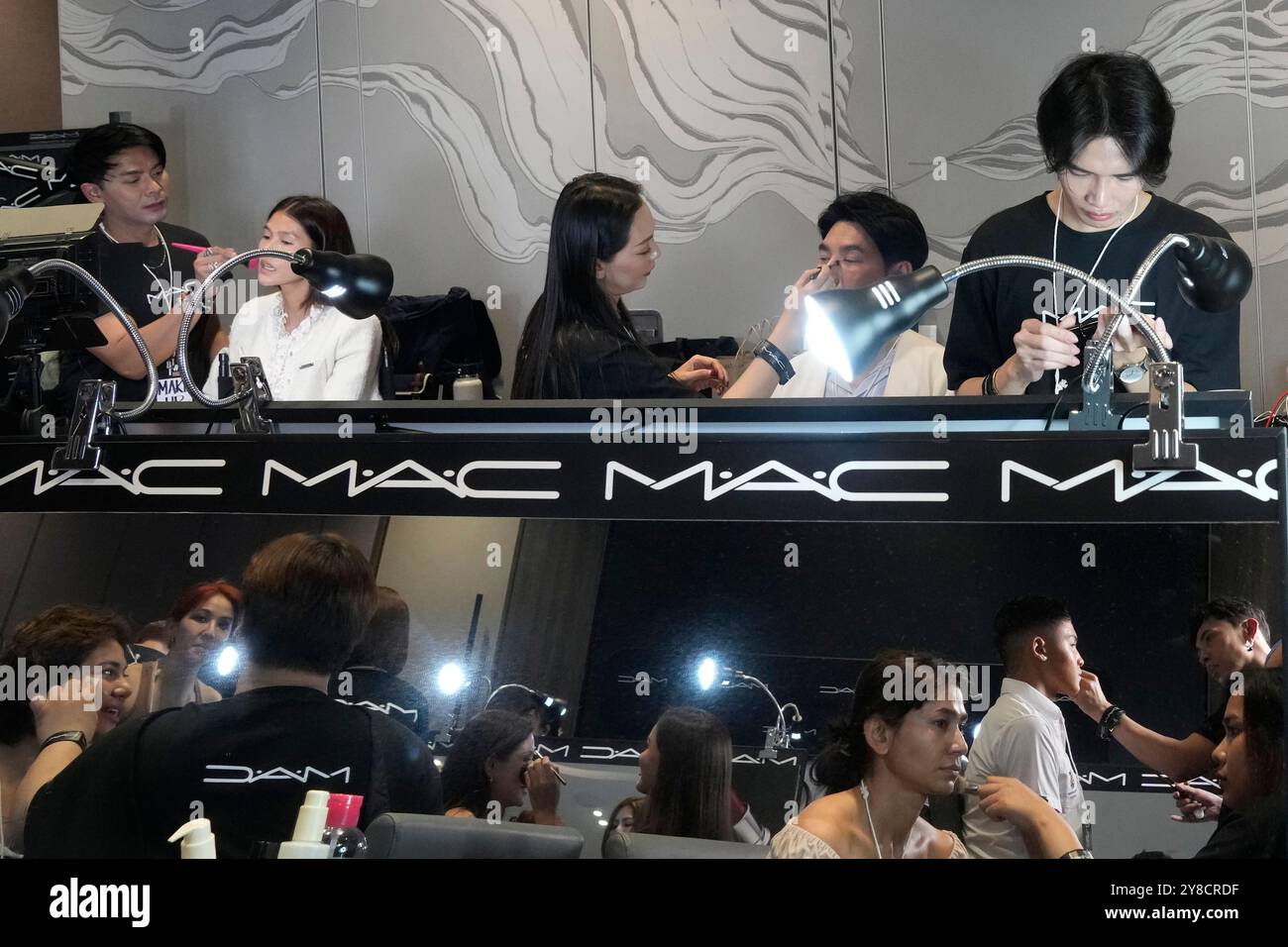 A makeup artist is reflected in a mirror as he gives the final touches ...