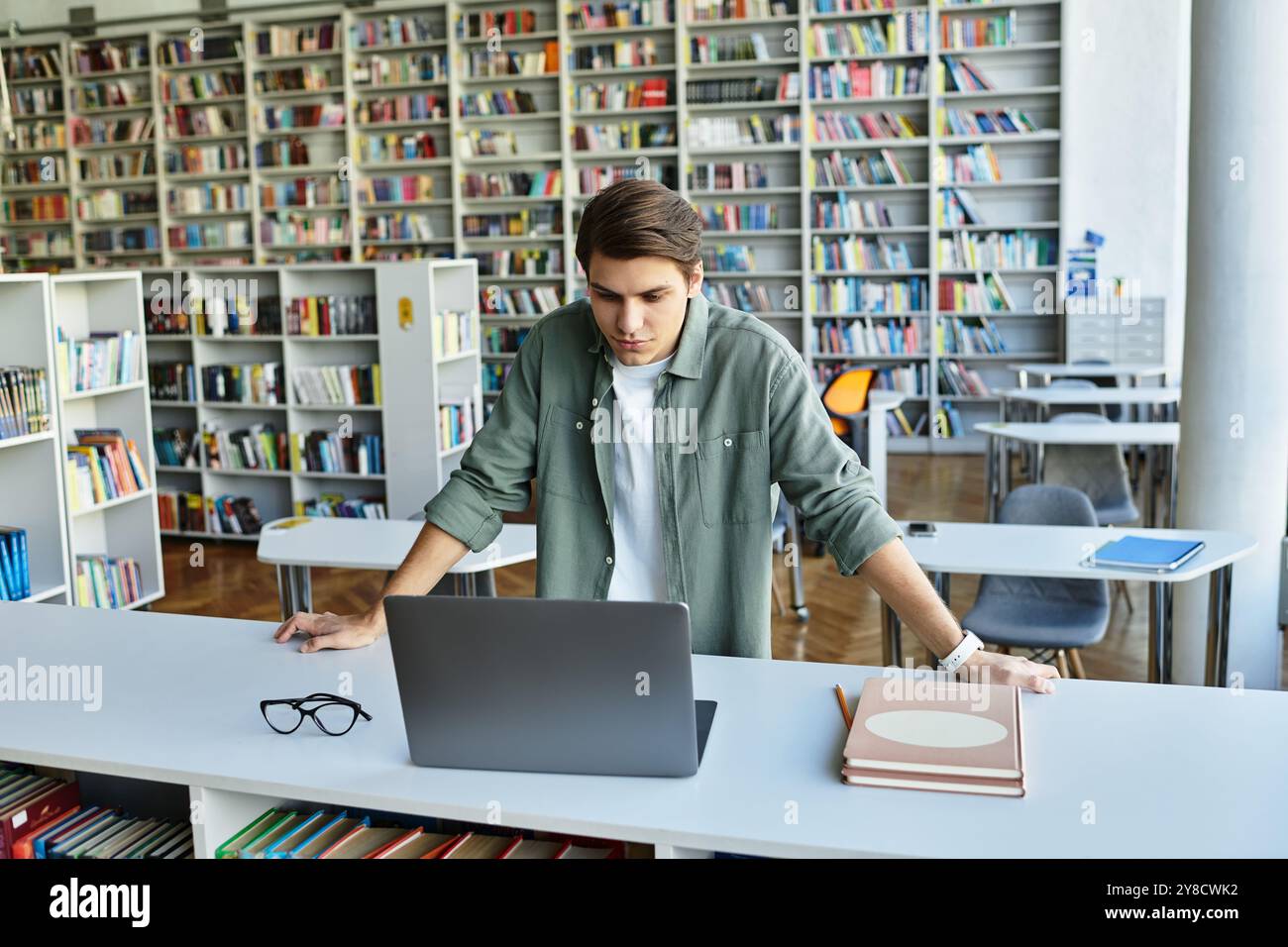 A focused student engages with his laptop amidst shelves of books in a library Stock Photo - Alamy