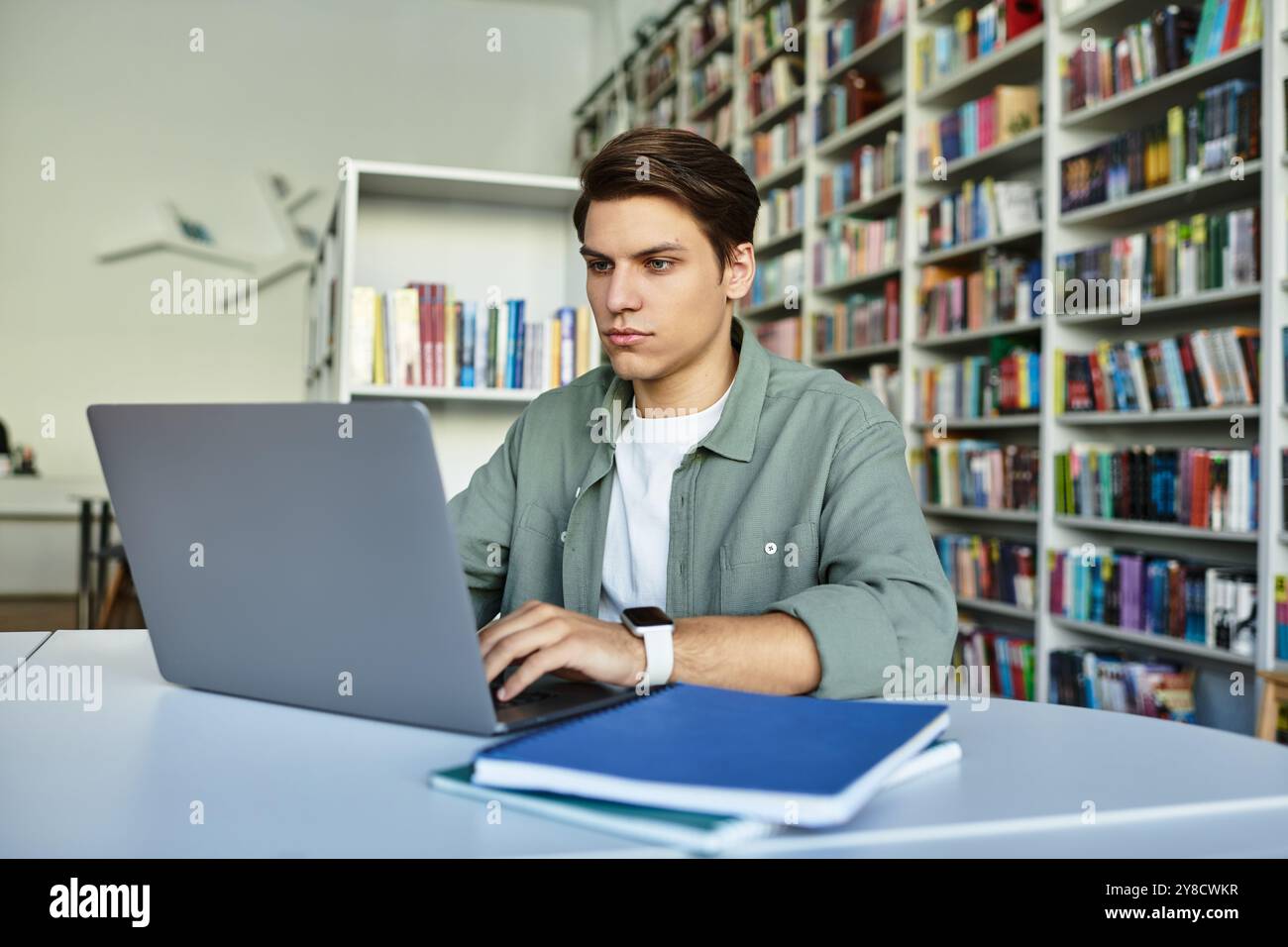A diligent student concentrates on his studies at a library desk filled ...