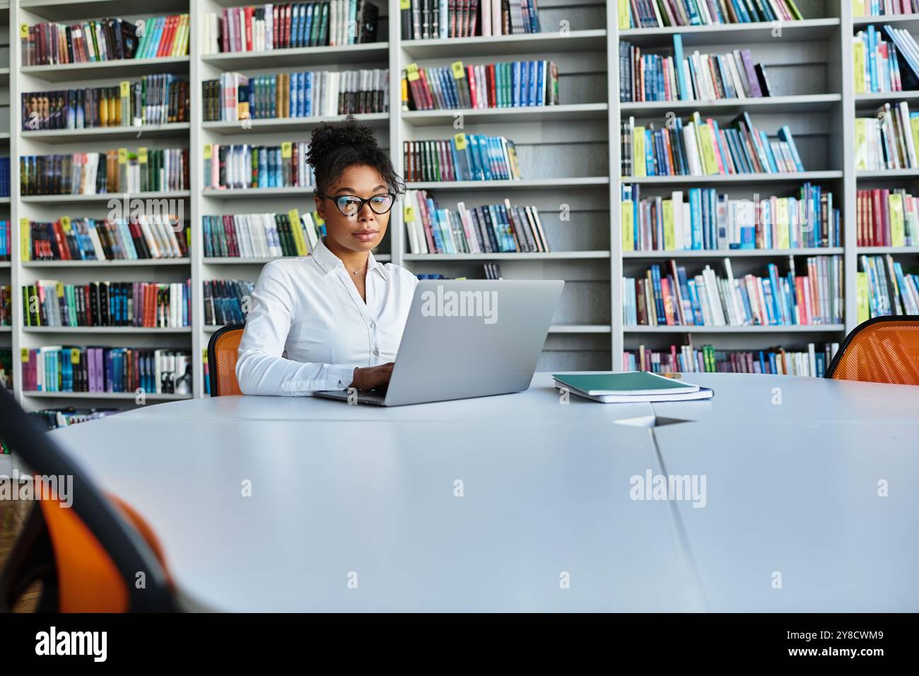An inspiring teacher works on her laptop in a colorful library full of ...