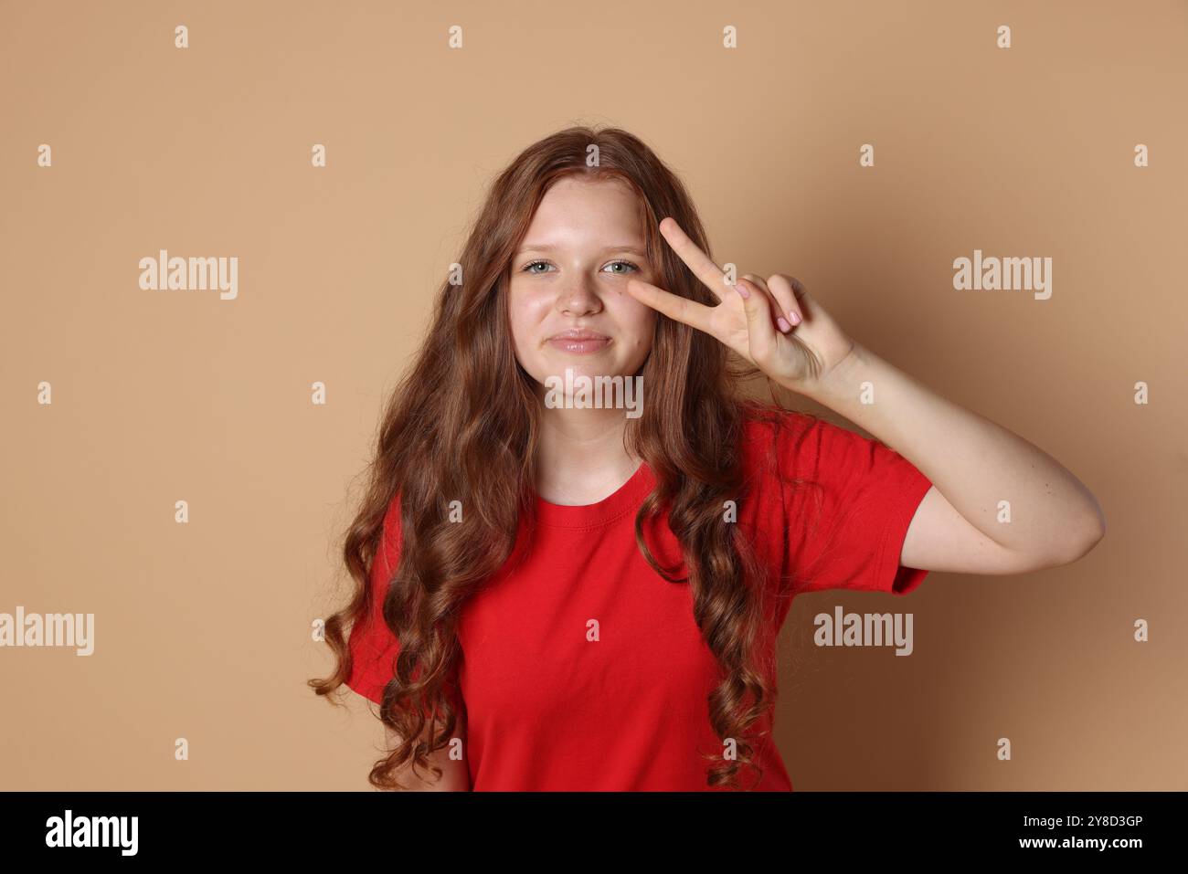 Cute teenage girl showing peace sign on beige background Stock Photo ...
