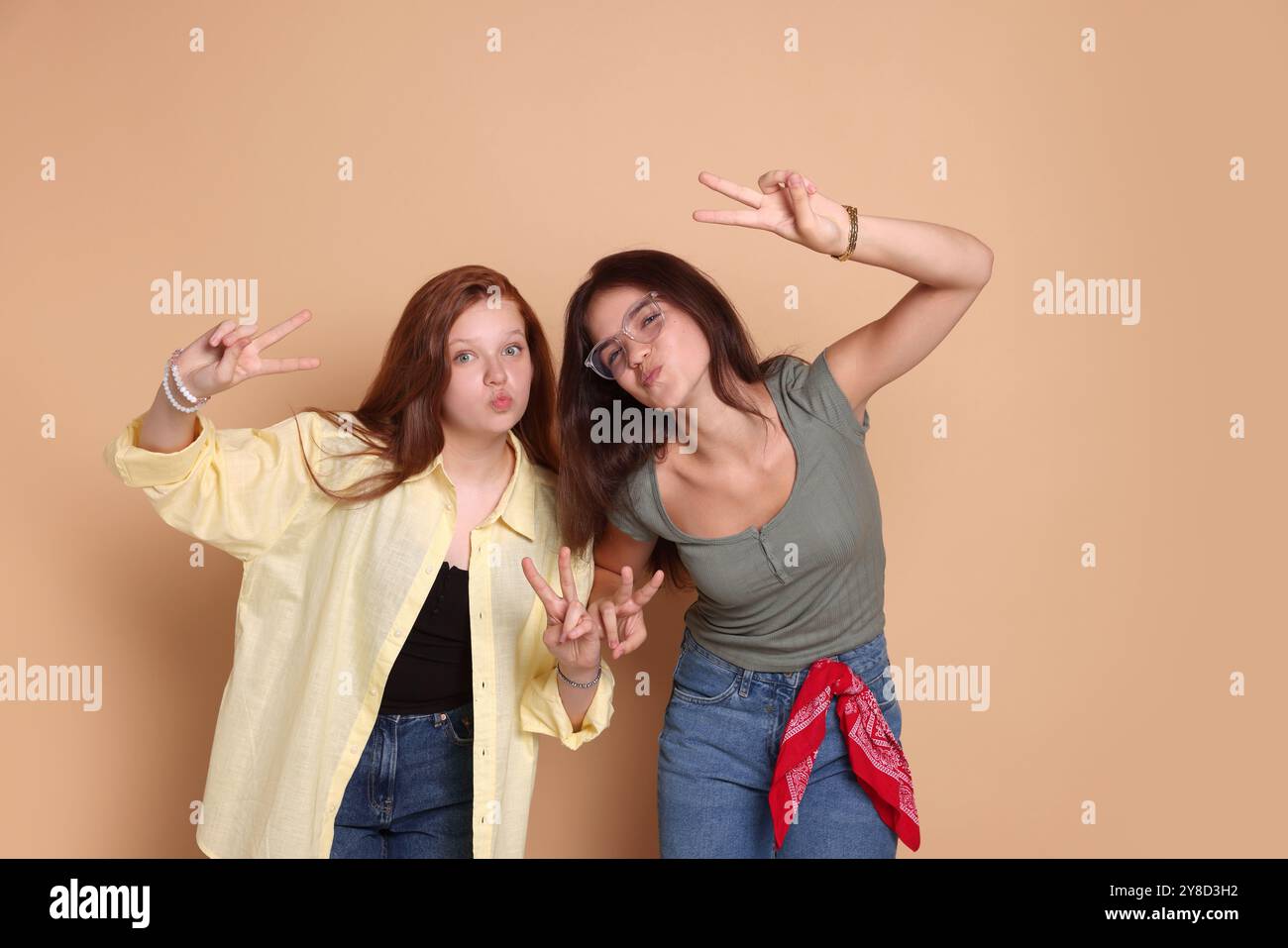 Cute teenage girls showing peace signs on beige background Stock Photo ...