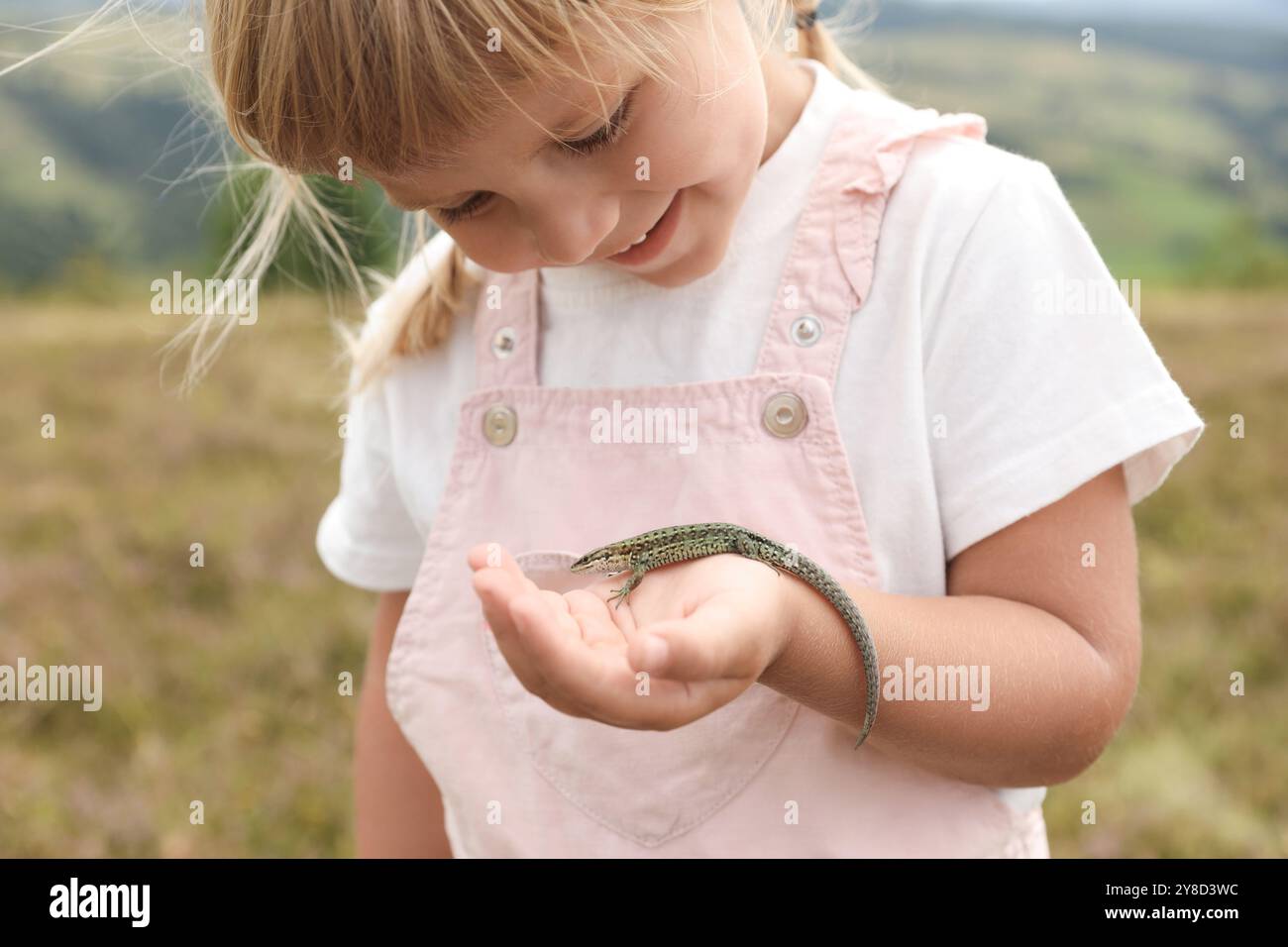 Smiling little girl holding lizard at field. Child enjoying beautiful ...
