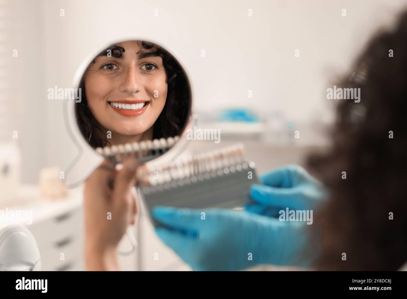 Patient looking in mirror while doctor holding teeth color chart in ...