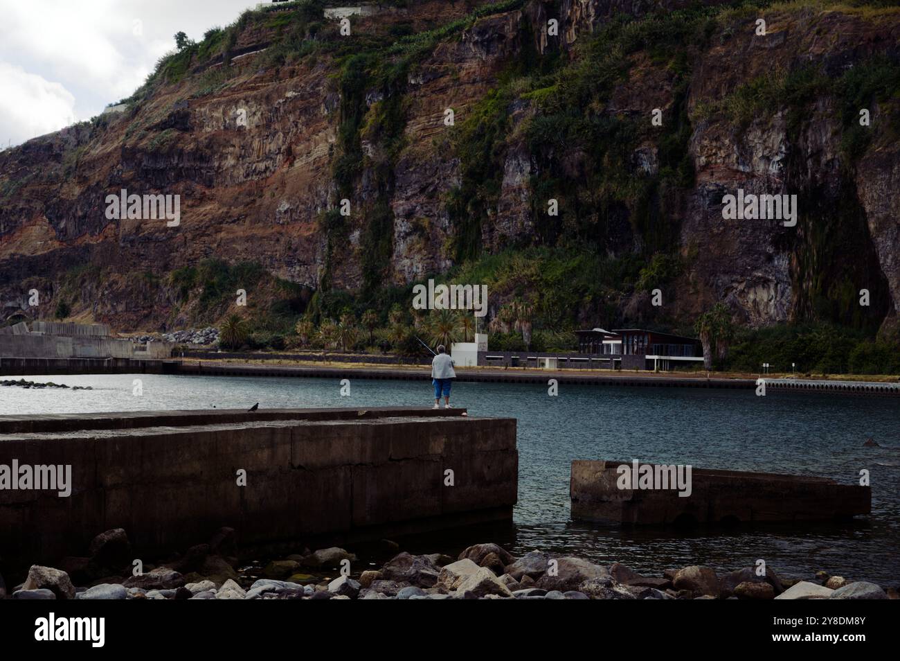 A solitary female fisher casts her line from a rugged concrete pier ...