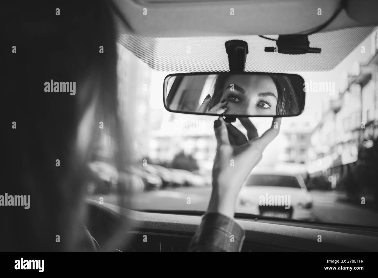 Young woman looking in rear view mirror and putting make up in car ...