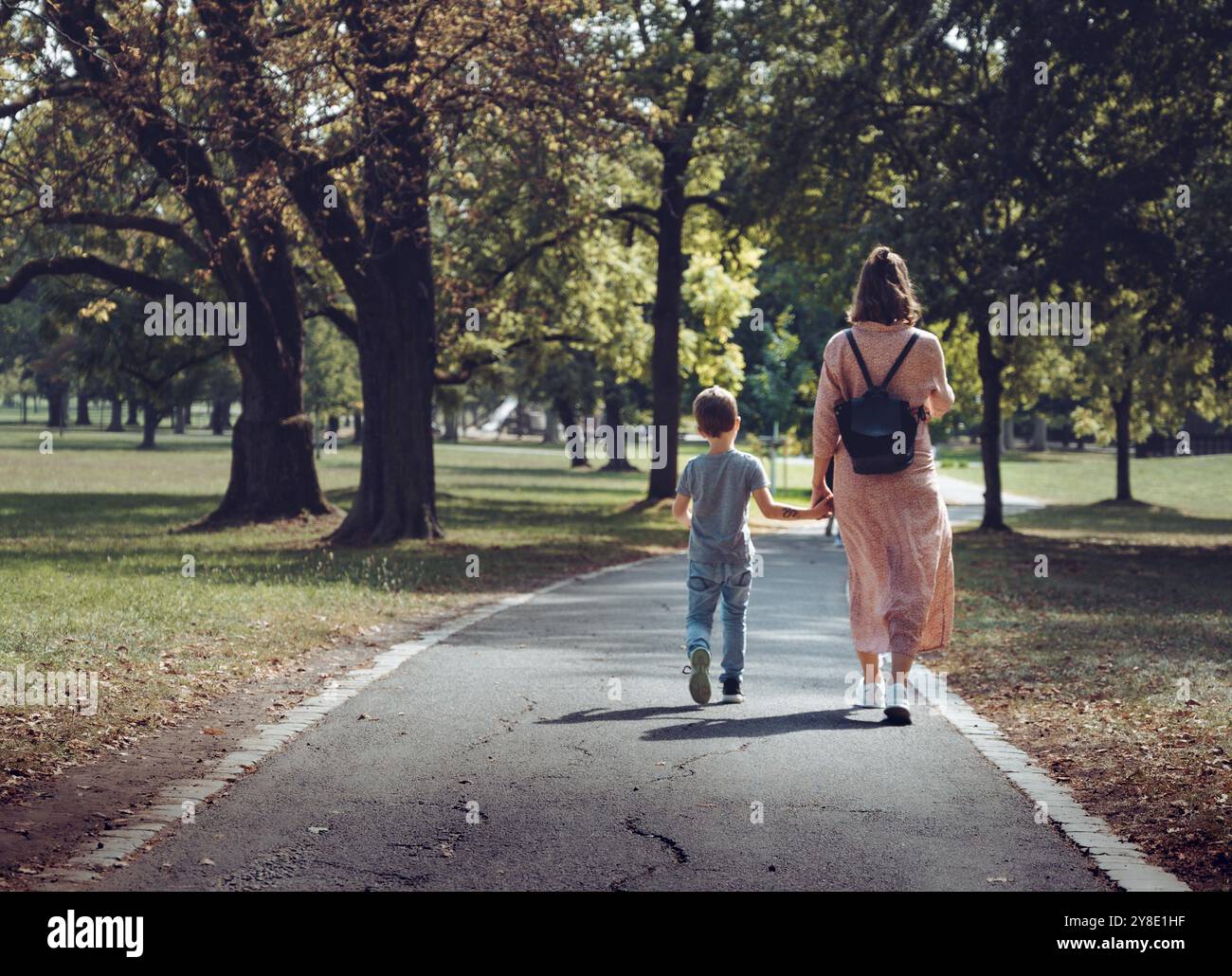 Mother and child walking along a path in the park, surrounded by trees ...