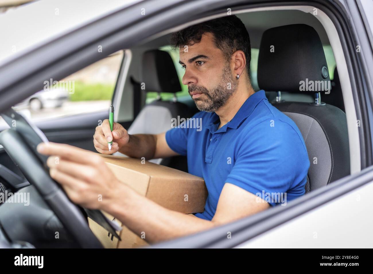 Delivery man checking a package ready to deliver sitting inside a car ...