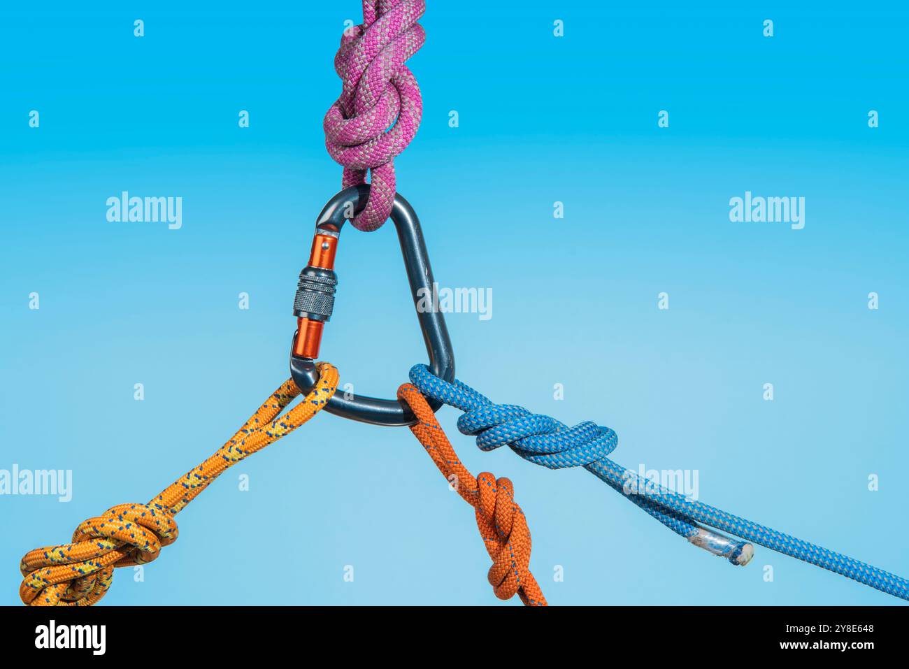 Close-up of a carabiner system securing 3 lines of rope against a blue ...