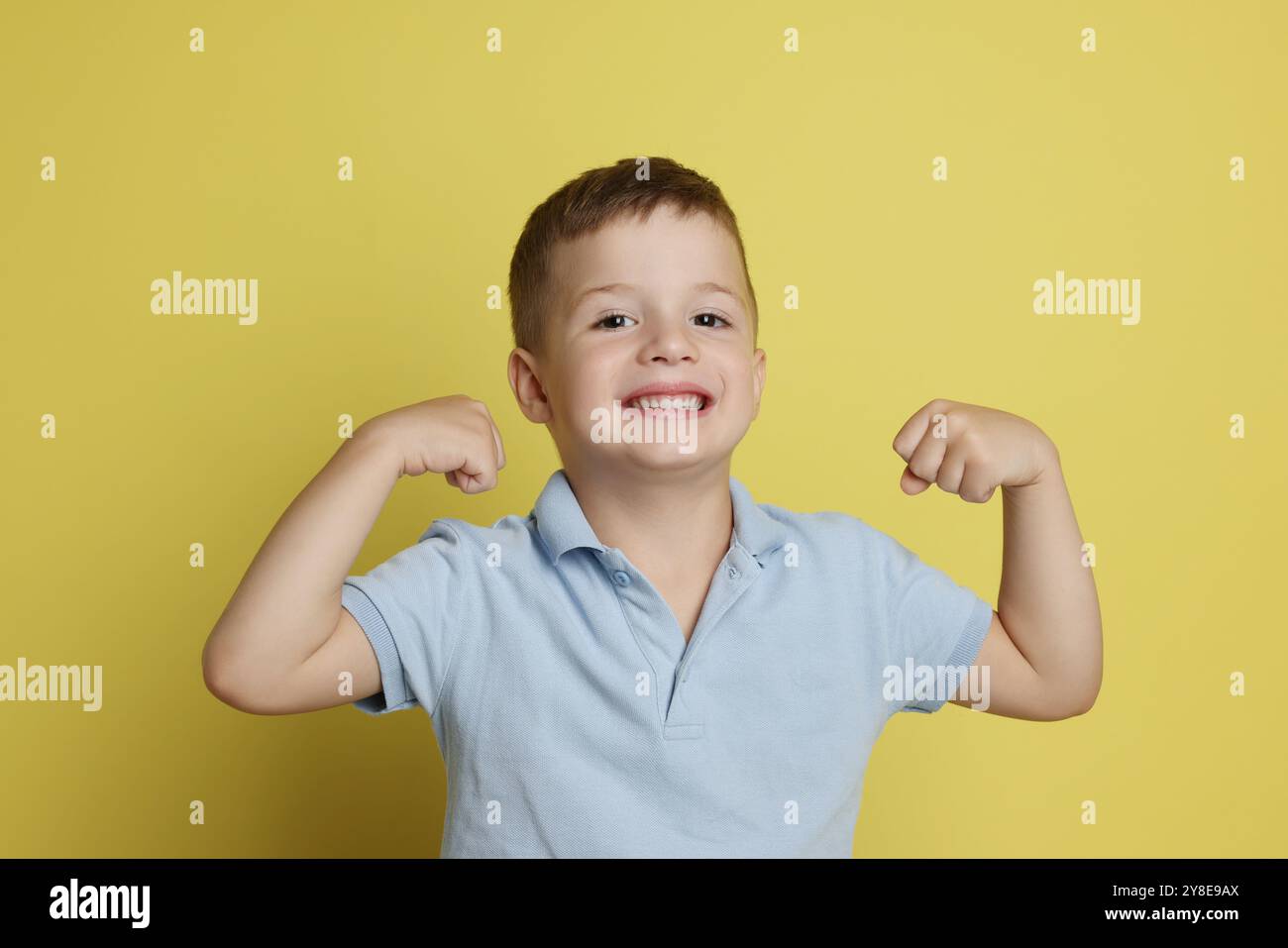 Cute little boy showing his biceps on yellow background Stock Photo - Alamy