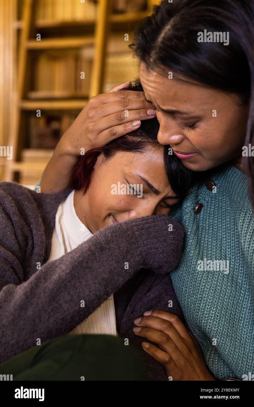 Sad biracial sisters sitting on couch and embracing in living room ...