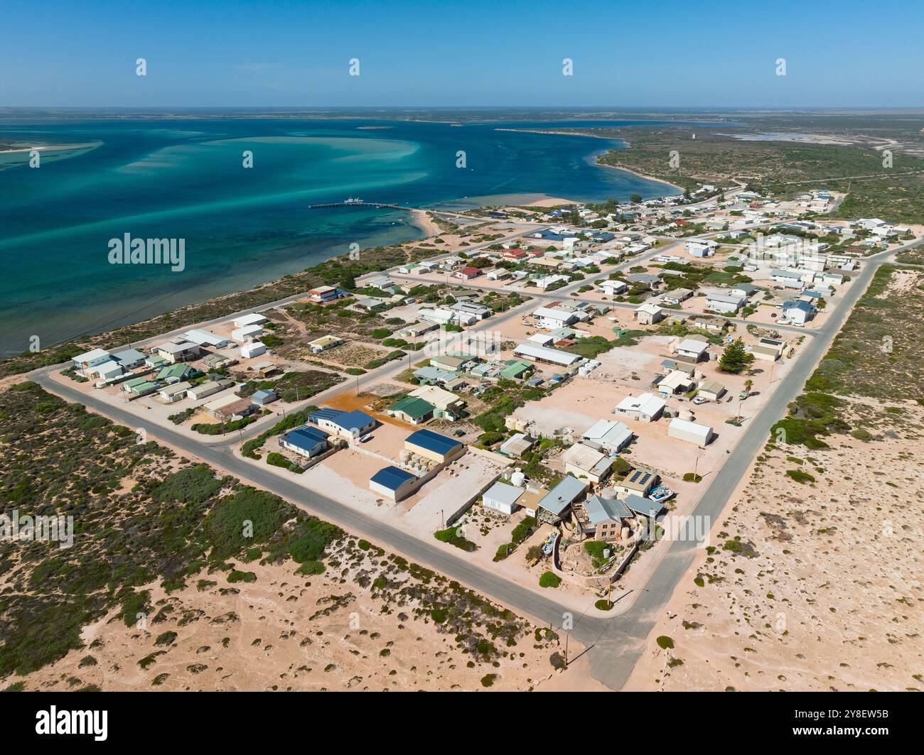 Aerial view over a small isolated coastal town alongside a calm bay sea ...