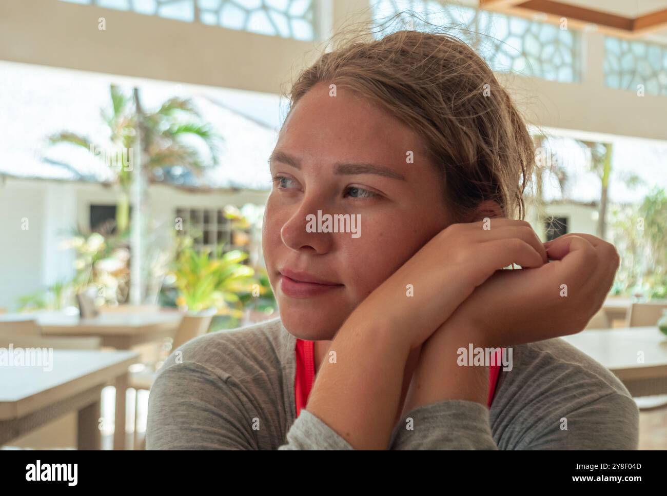 A young woman sits at a cafe table, resting her chin on her arms and ...