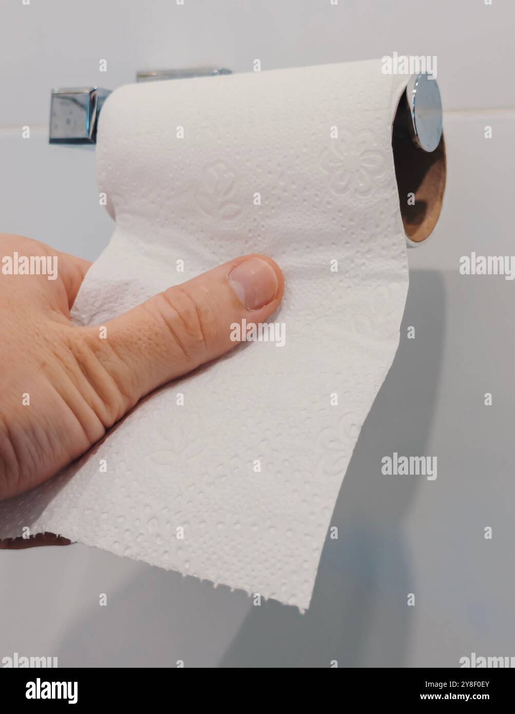 A hand pulls a sheet of toilet paper from a roll mounted on the wall in ...