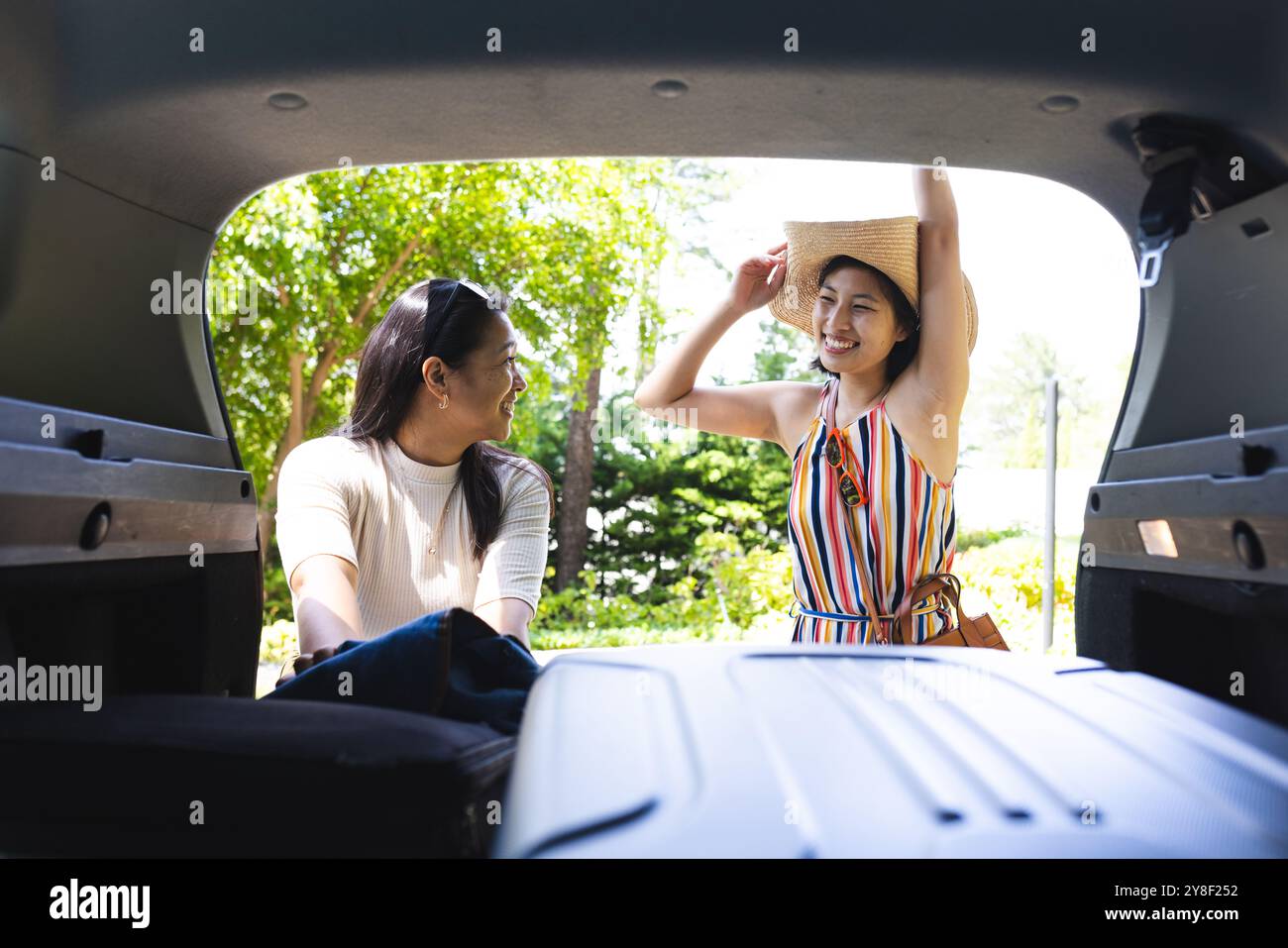 Happy asian female friends packing luggage in car and talking in garden ...