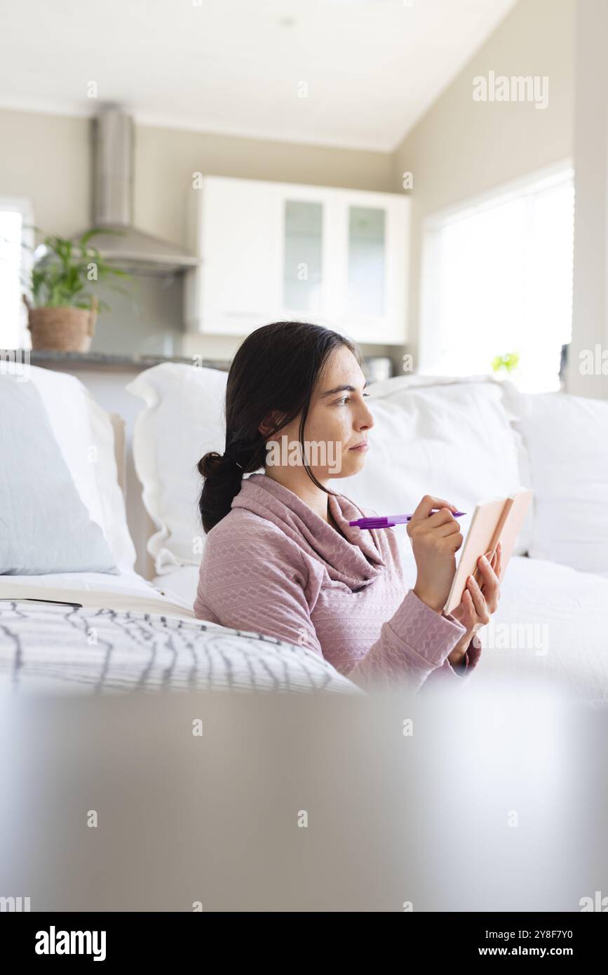 Caucasian young woman thinking and writing in notepad while relaxing by ...