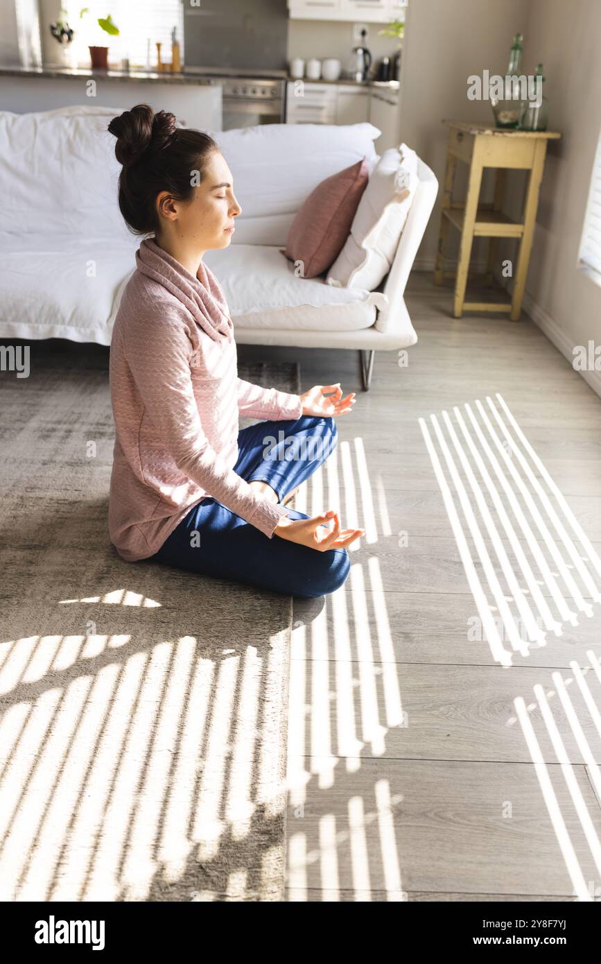 Side view of caucasian young woman meditating while sitting on floor in ...