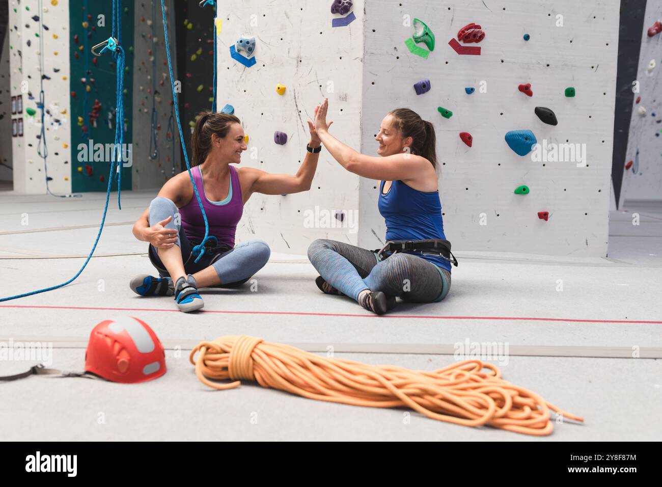 Two caucasian women talking and giving high five sitting on floor at ...