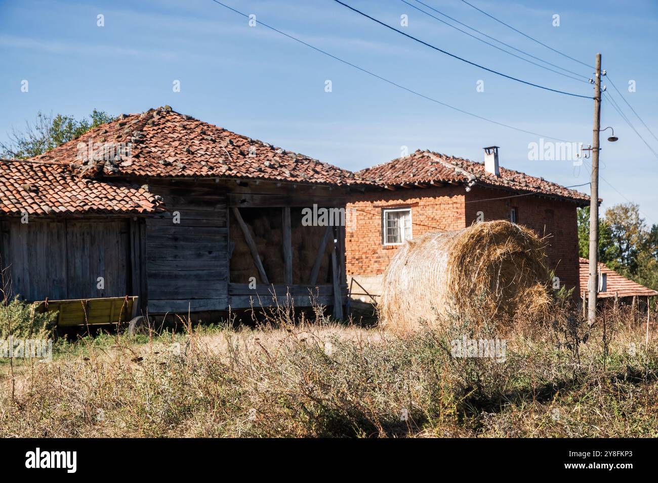 Old rural farmhouse with round hay bale in countryside in autumn time ...