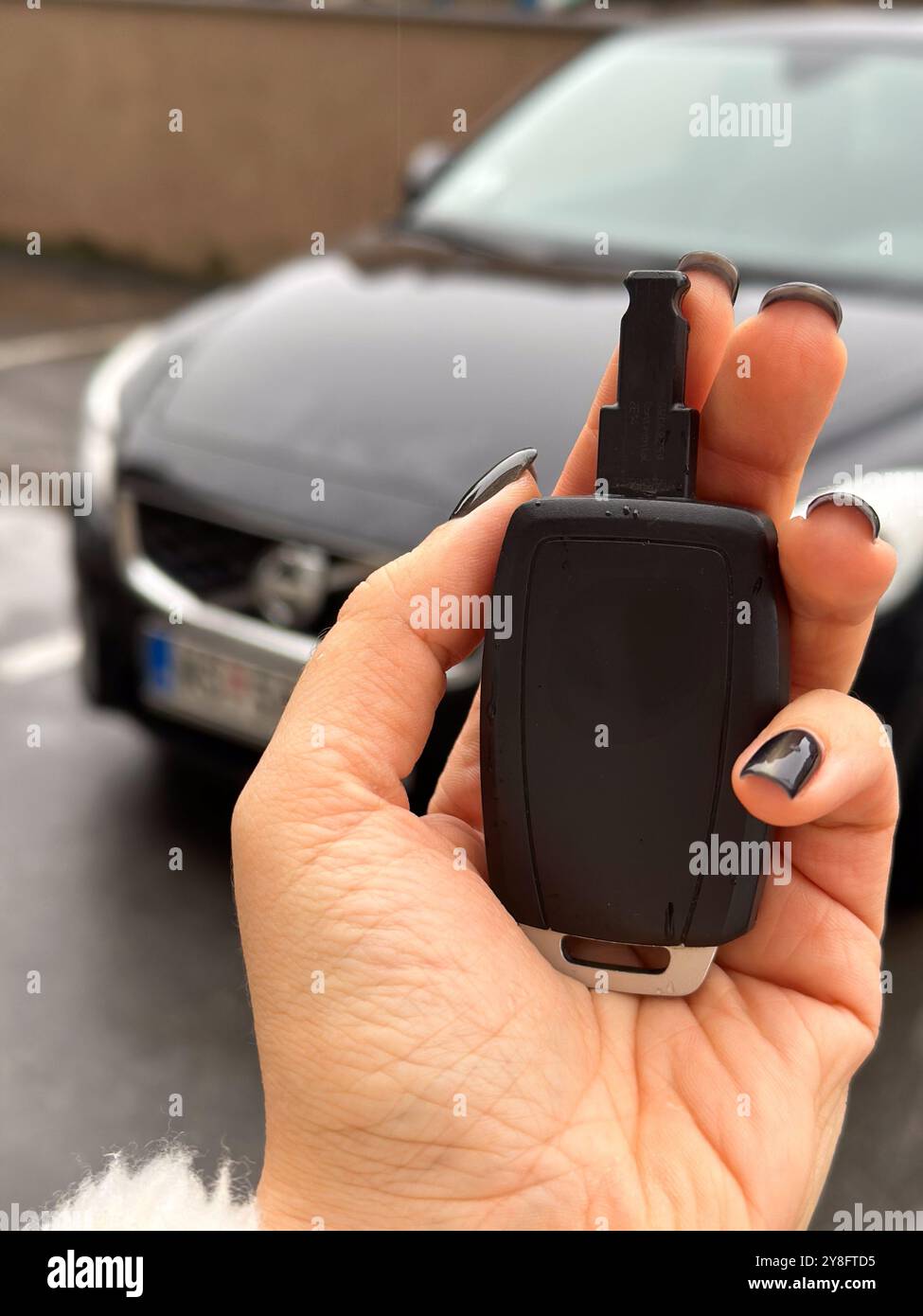 Woman's hand holding a car key fob in front of a black modern car on a ...