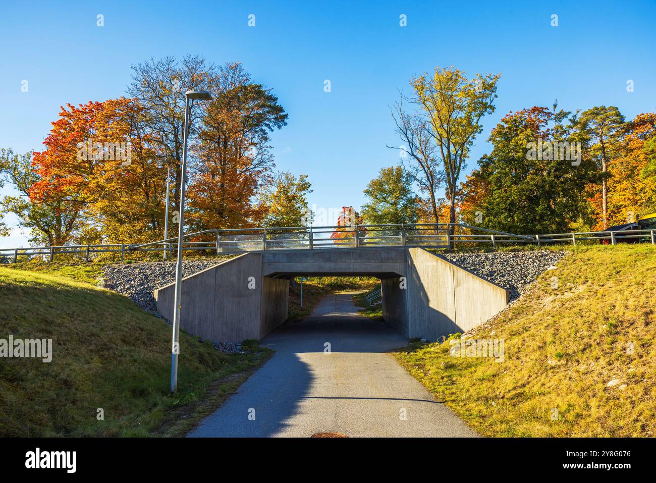 Concrete pedestrian underpass beneath road, with autumn trees and clear ...