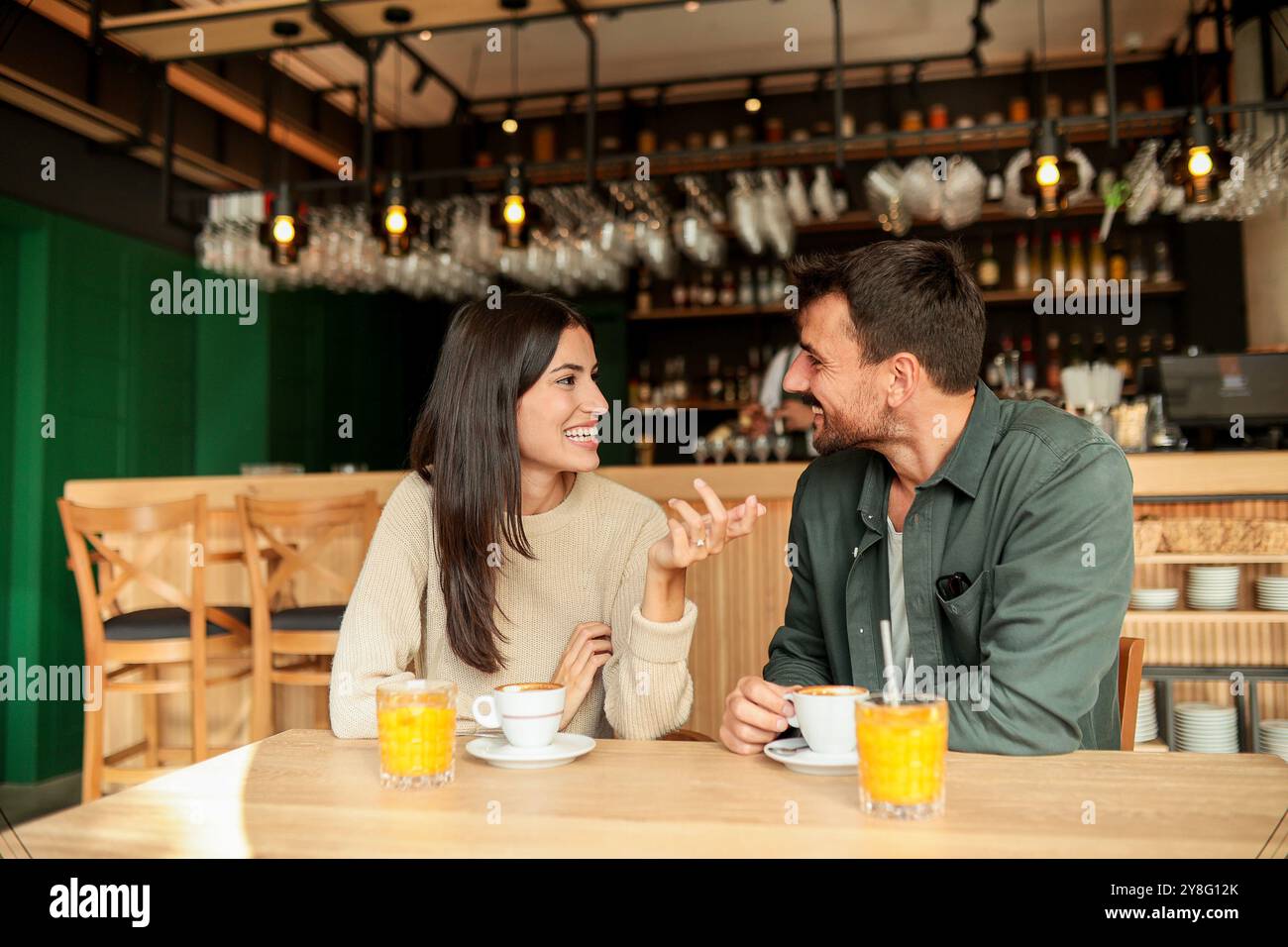 Couple shares a joyful moment at a stylish café, sipping coffee and ...