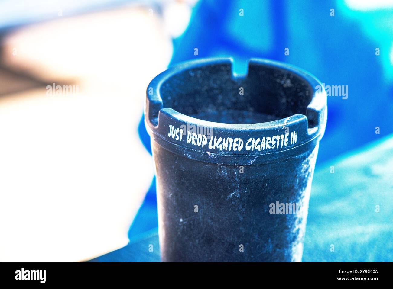 A close-up photo of an ashtray featuring a sign that reads "Just Drop ...