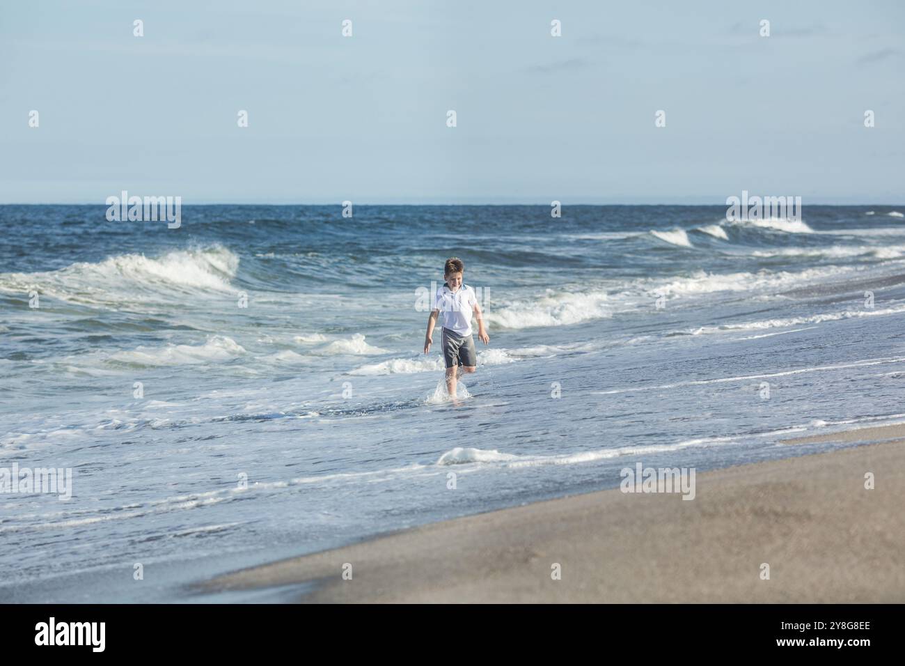 Teenage male walking into the surf on a tropical beach. Sunny day with ...