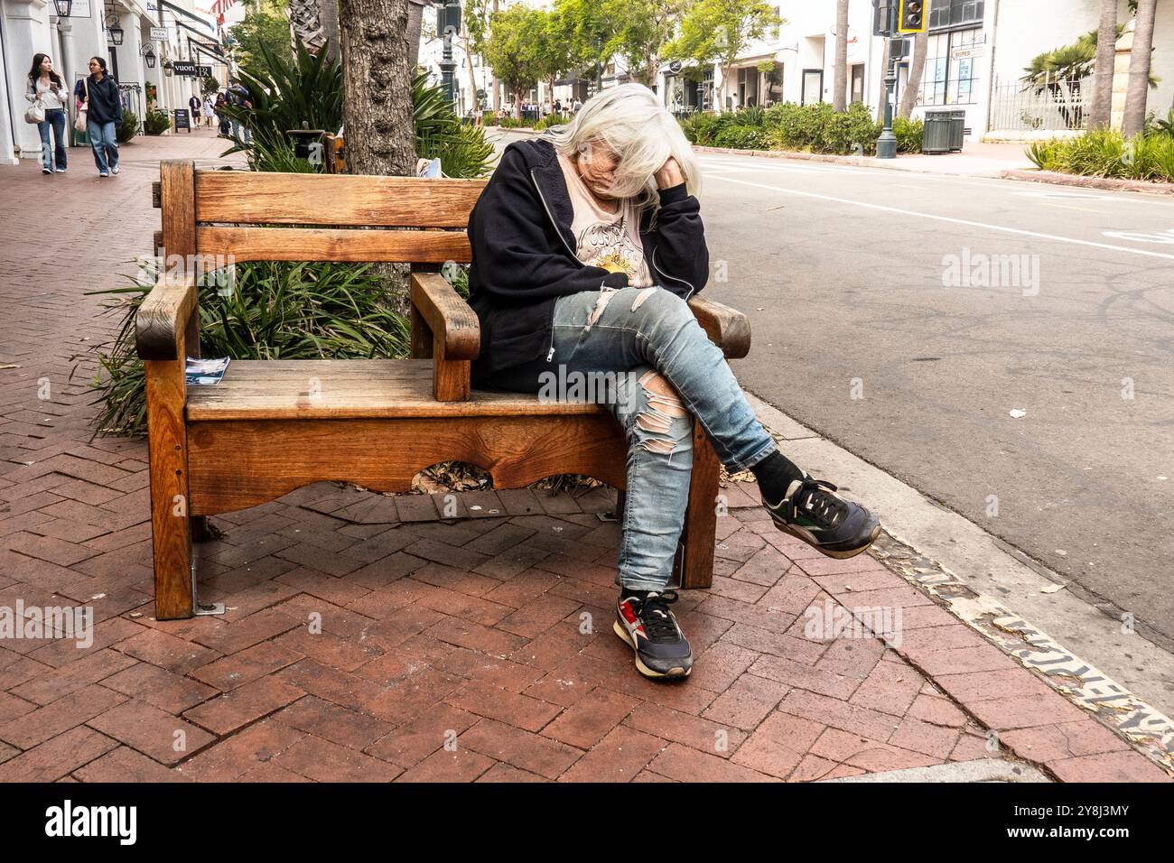 A grey haired older homeless women is napping on a city bench on State ...