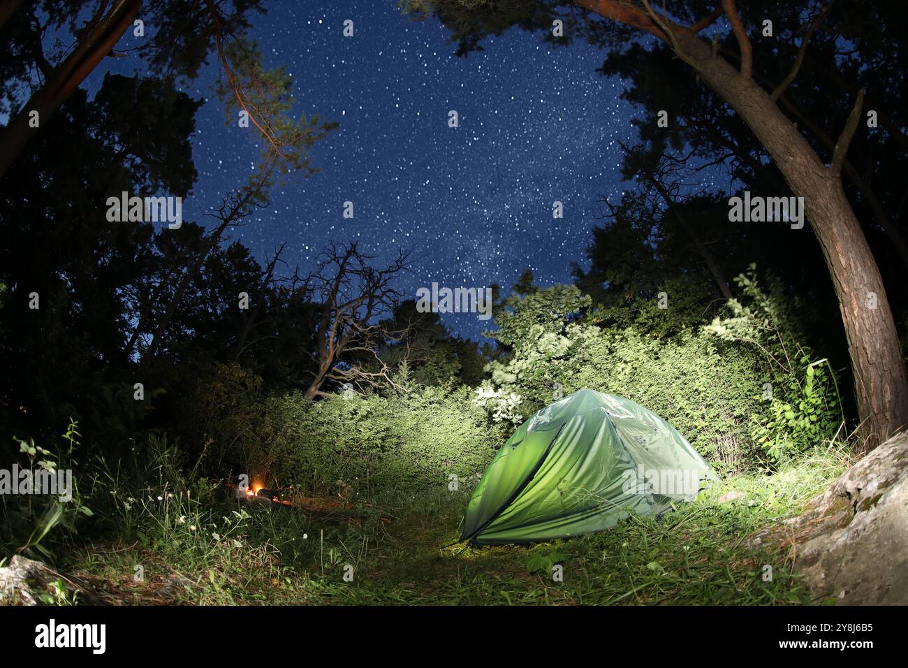 Modern camping tent and bonfire in forest at night. Fisheye lens effect ...