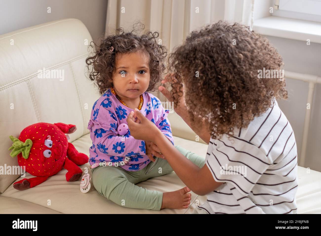 Sibling bonding moment on a couch, young child dressed in a floral ...