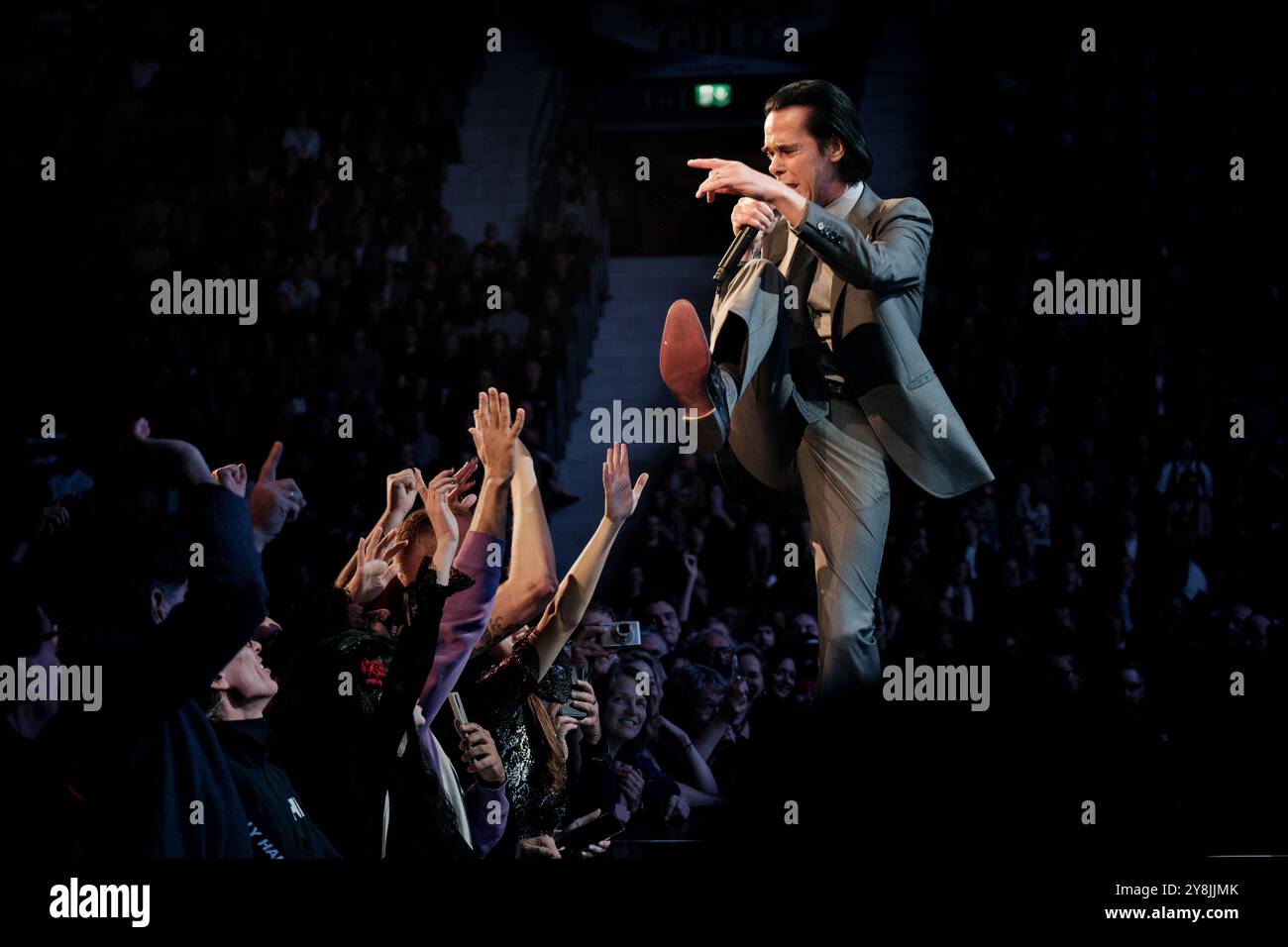 Nick Cave kicking in the air while running on stage with the Bad Seeds ...