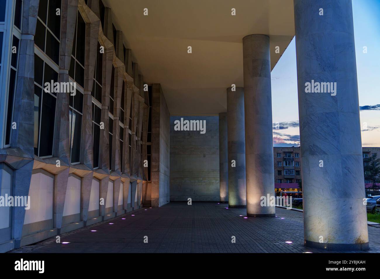 The entrance of a modern building with large columns is illuminated at ...