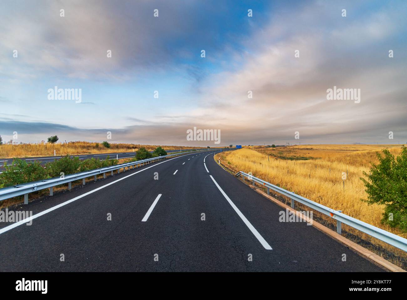 Empty highway between yellow grain fields and a dramatic sky at dawn ...