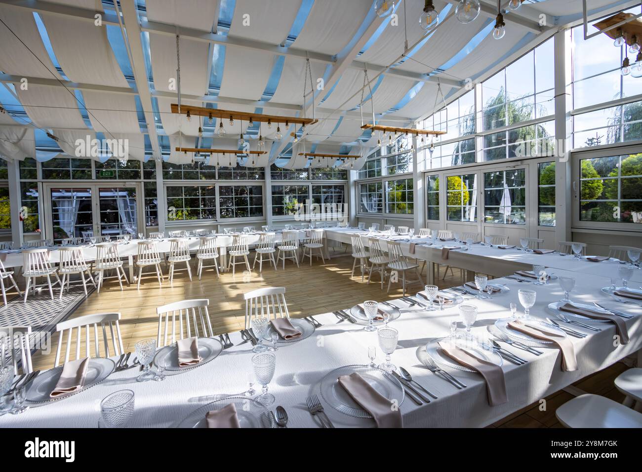 A bright, glass-walled banquet hall with tables covered with white ...