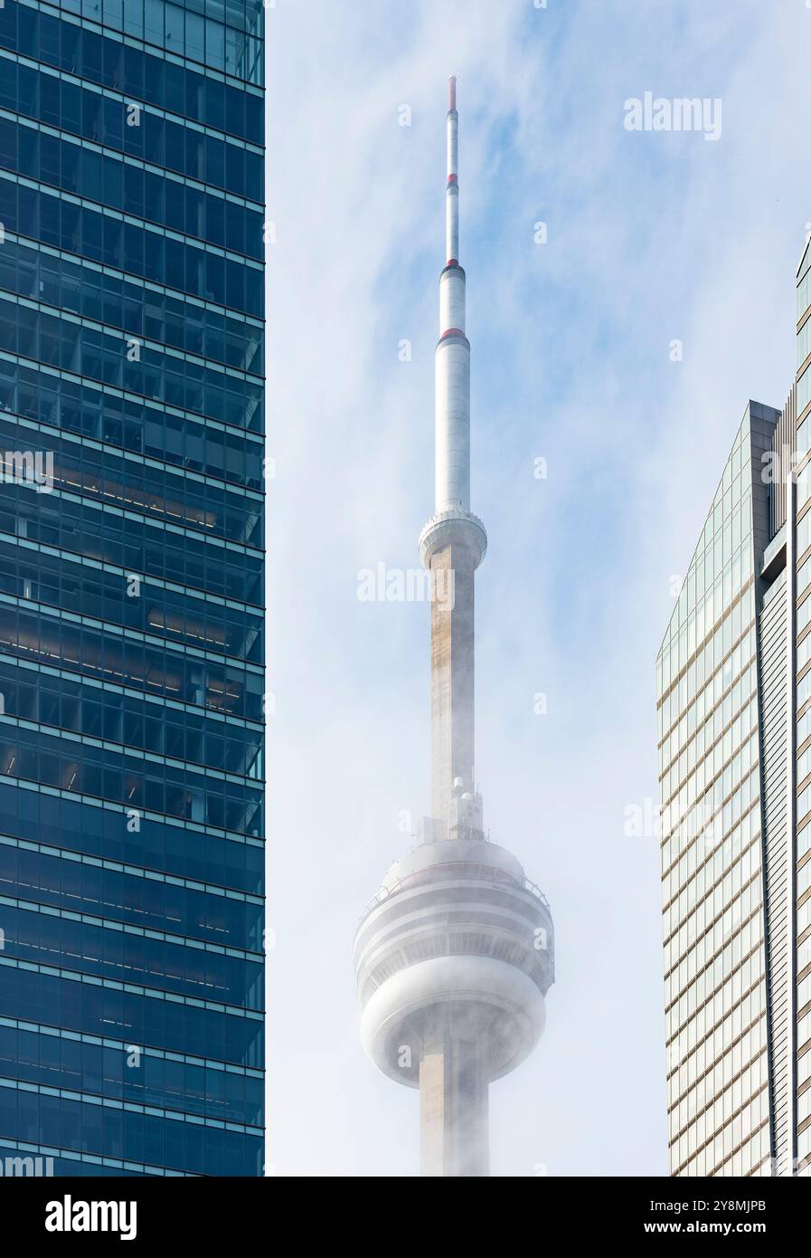 The CN Tower in Toronto emerges from the mist between two skyscrapers ...