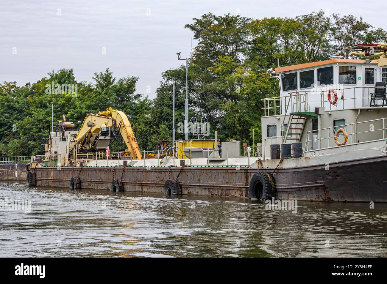 Old industrial vessel with an excavator on deck, anchored at small quay ...