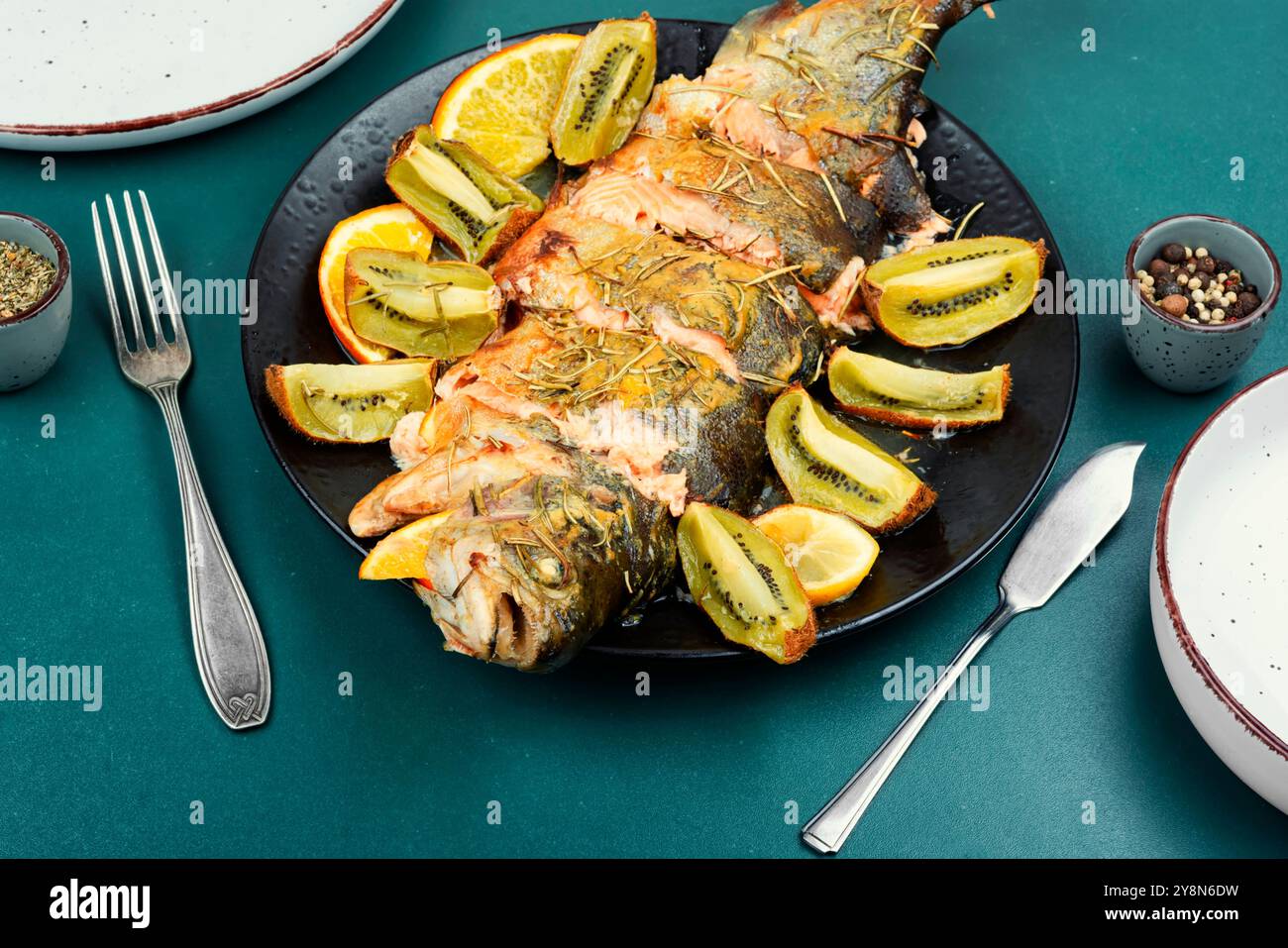 Roasted fish is served with kiwi slices and orange. Seafood dinner ...